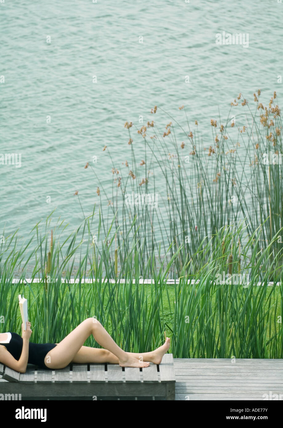 Young woman lying on lounge chair, reading Stock Photo - Alamy