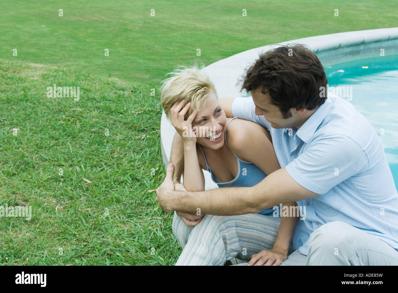 Couple sitting by pool, smiling at each other Stock Photo - Alamy