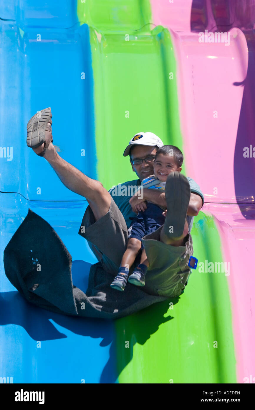 Hispanic Father Holding His Son In His Arms As They Slide Down A