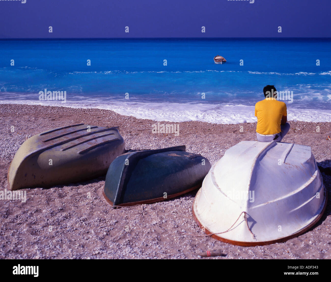 Turkish man sat relaxing looking at the deep blue water at Olu Deniz ...