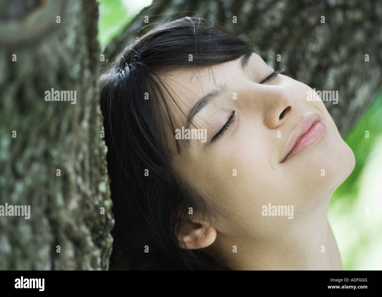 Woman with head against tree trunk, eyes closed, smiling Stock Photo ...