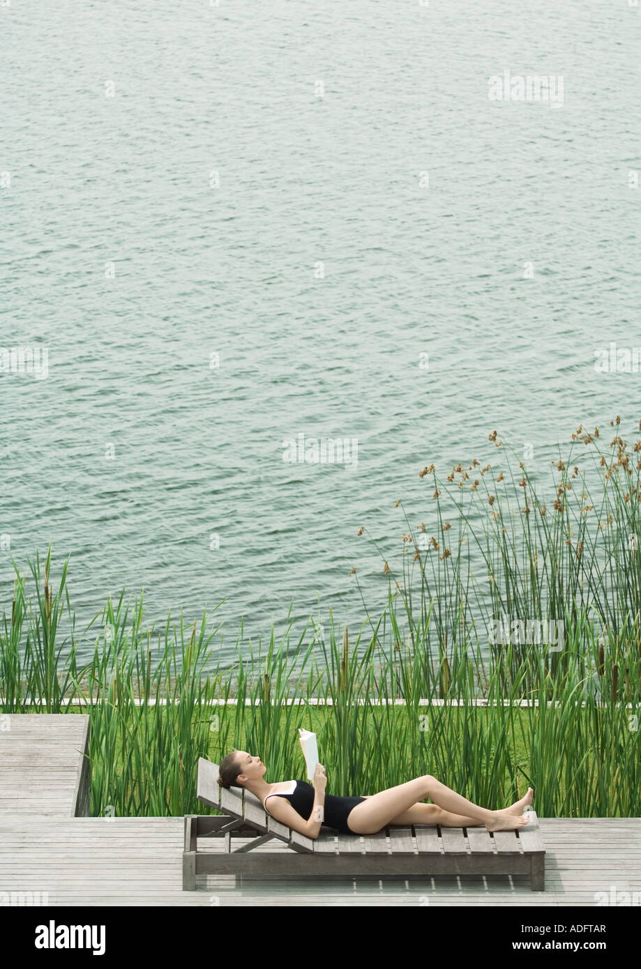 Woman reclining on lounge chair, reading, next to lake Stock Photo - Alamy