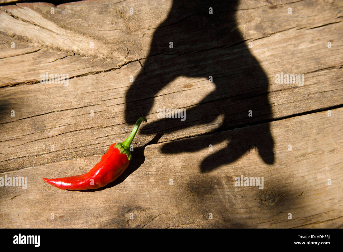 Male hand shadow cast over wooden table as if holding a red pepper ...