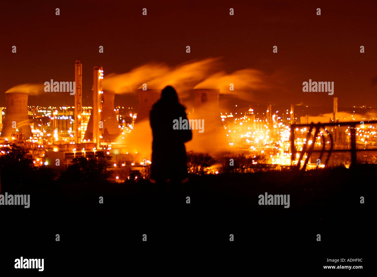 Young female figure silhouetted against oil refinery at night Stock ...