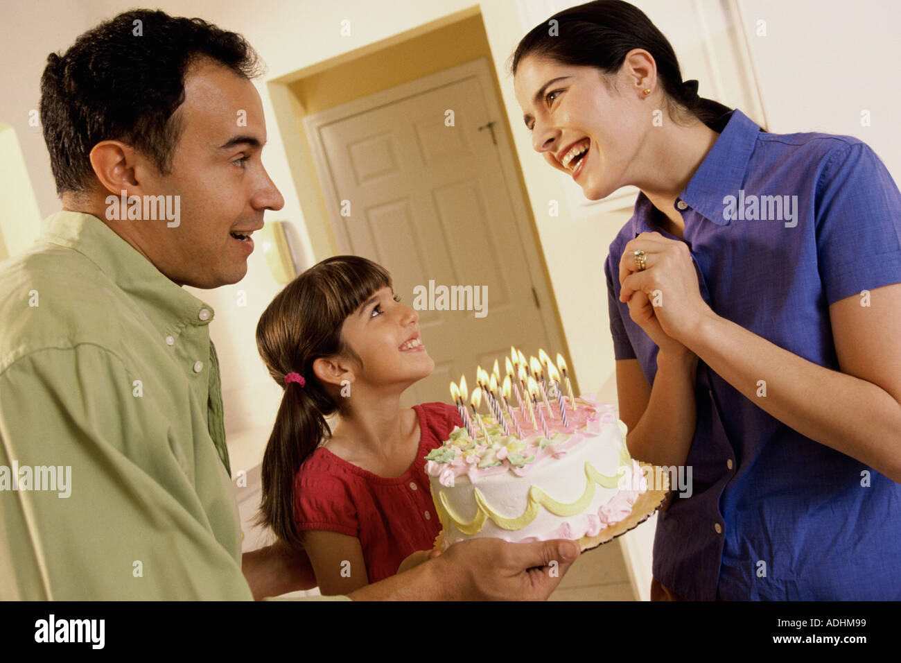 Girl standing in front of a birthday cake with her parents Stock Photo ...