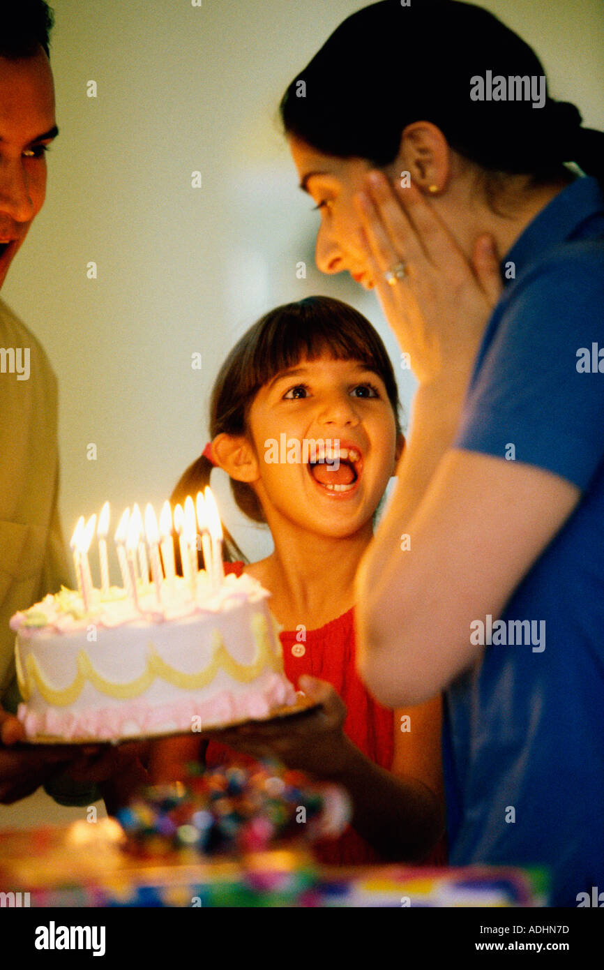 Girl standing in front of a birthday cake with her parents Stock Photo ...