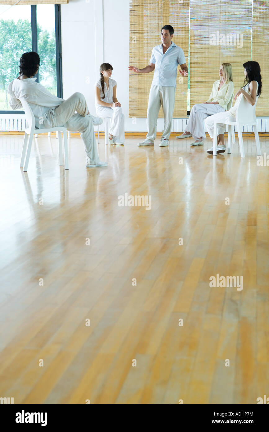 Group therapy, adults sitting in circle while one man stands in center ...