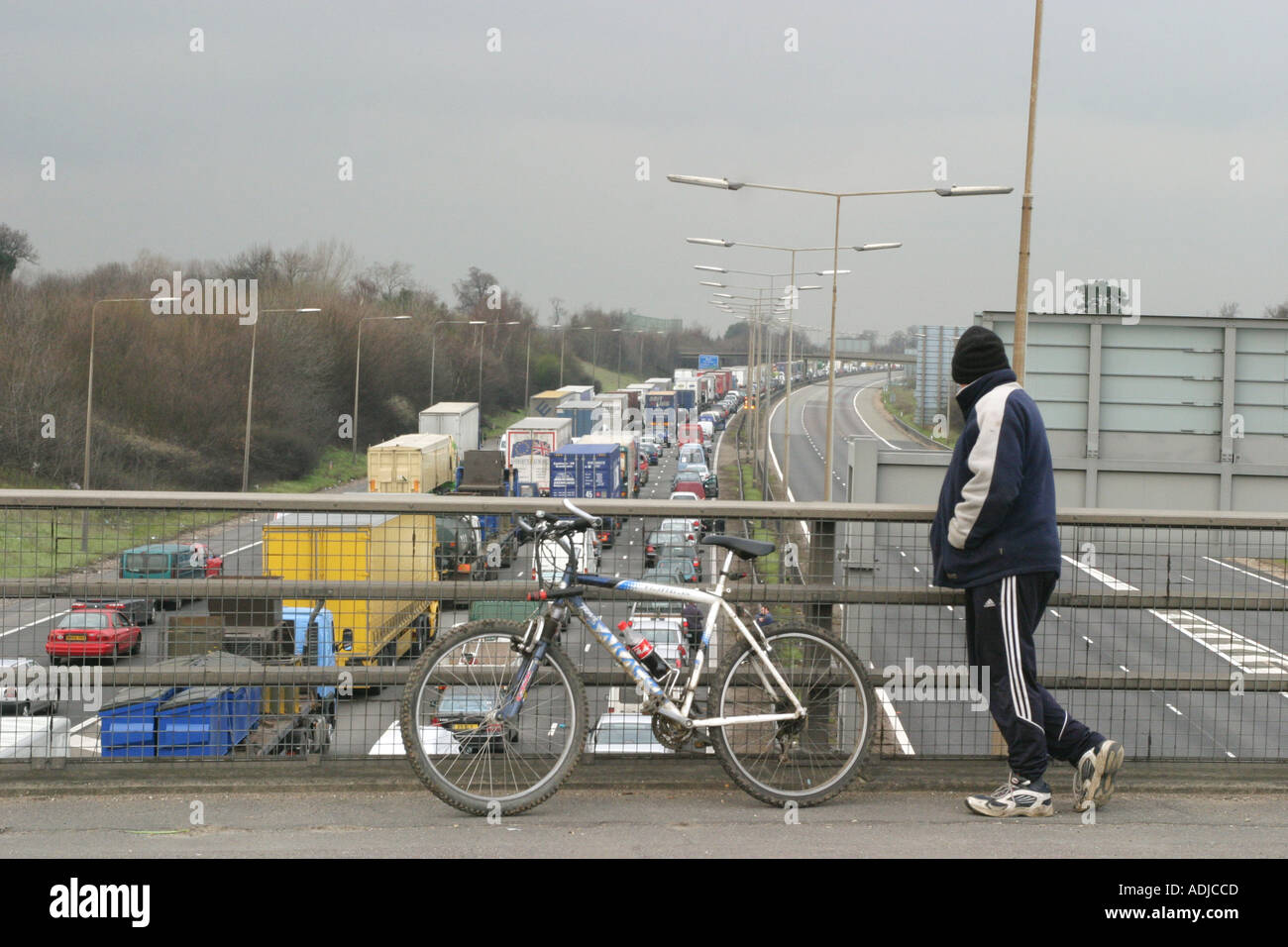 Cyclist standing on a bridge watching a traffic jam on the m25 motorway ...