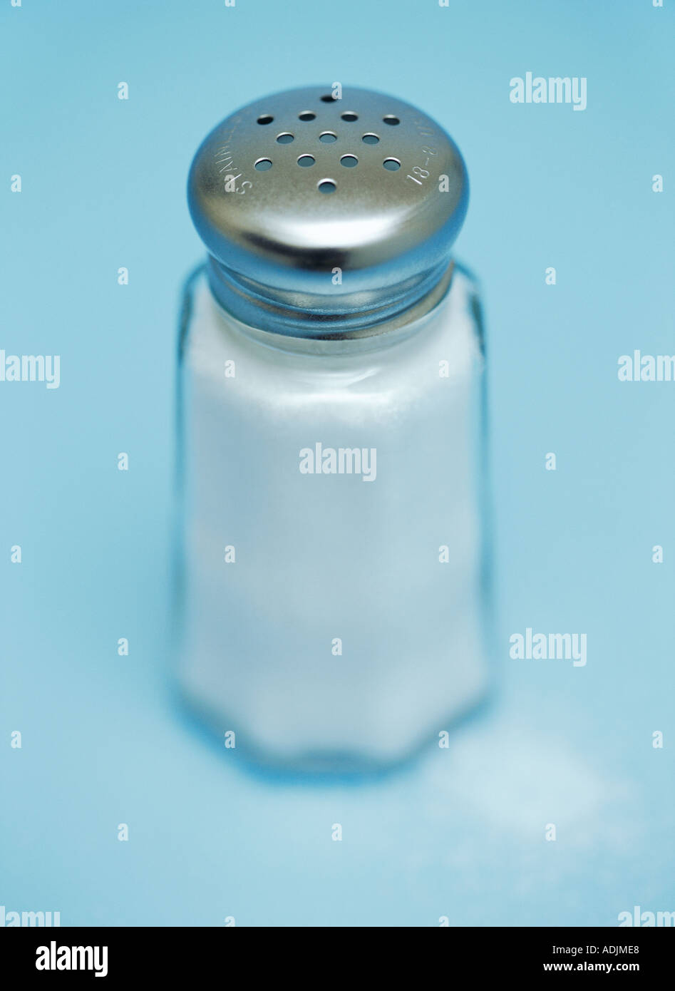 Salt cellar with salt spilling out onto pale blue background Stock ...