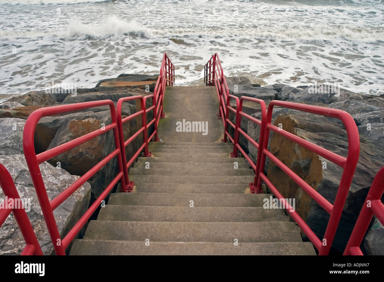 A red handrail and steps leading to the sea on an overcast day Stock ...