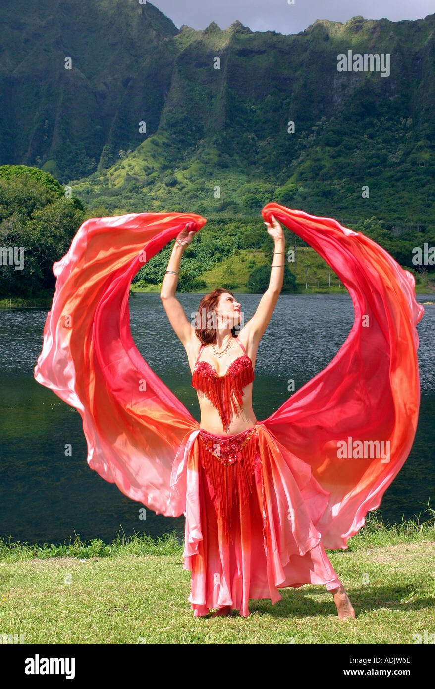 Belly dancer with red veil arms outstretched in tropical setting Stock ...