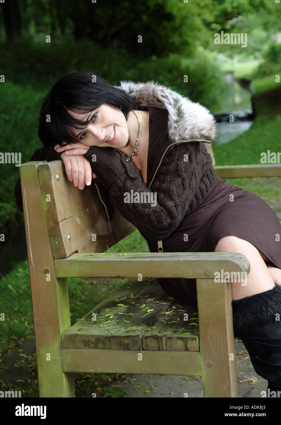 Sole young female model sits relaxed and smiling on park bench at ...