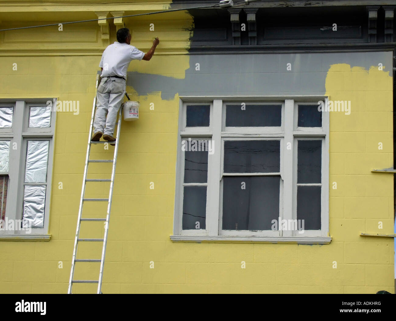 "Painter up a ladder applying "yellow paint' to an "apartment building ...