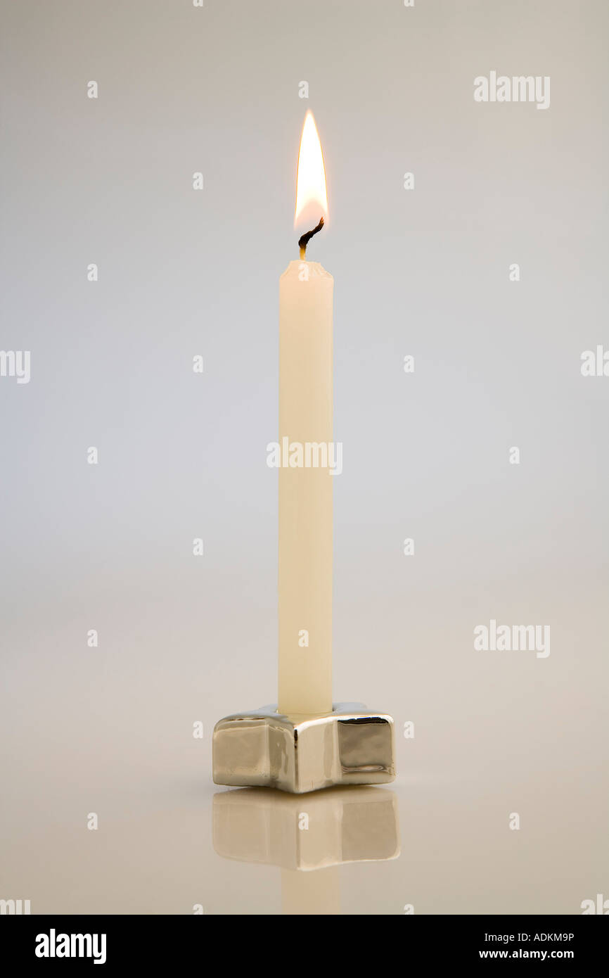 Closeup of one lit white candle with silver star Christmas base on ...