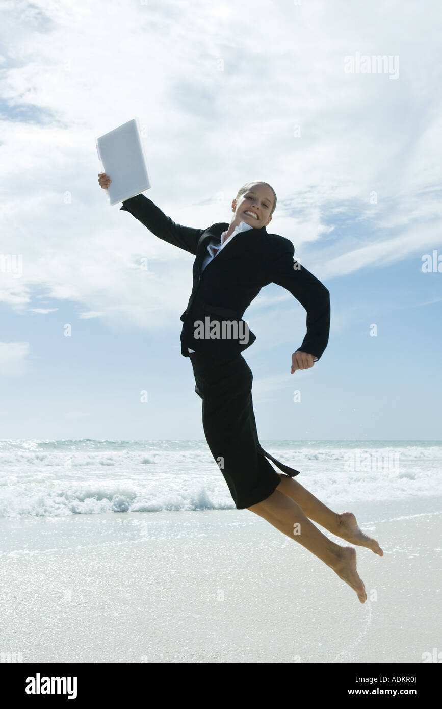 Businesswoman jumping in air on beach, smiling at camera Stock Photo ...