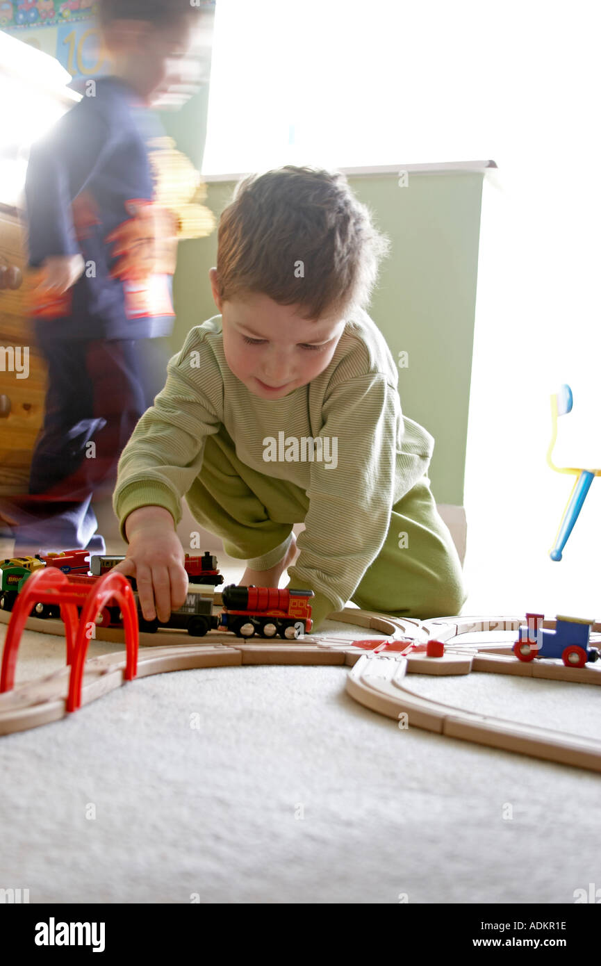 Young boy playing with a train set toy in his bedroom while his brother ...