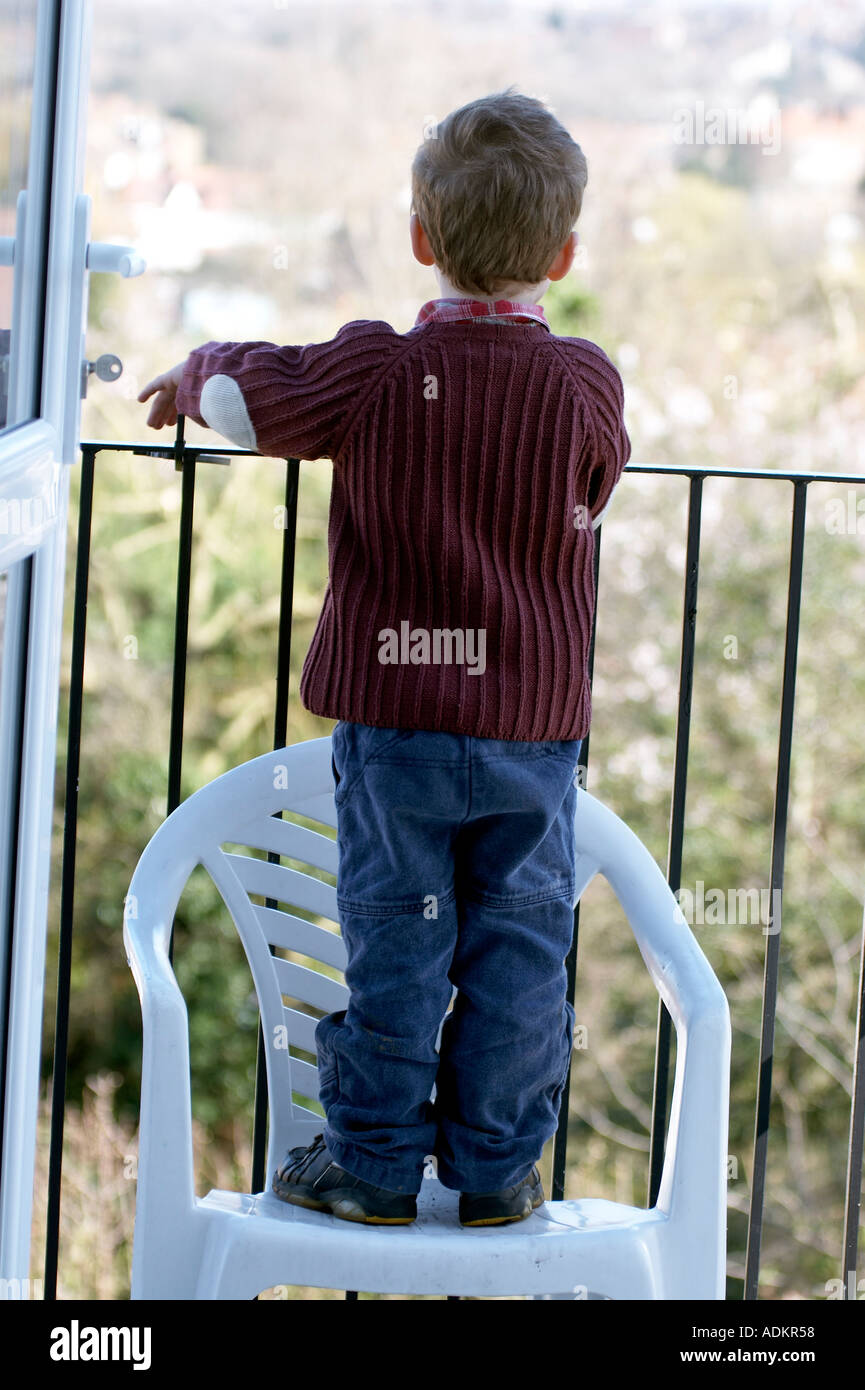 Young boy standing on a chair looking out over a balcony railings in ...