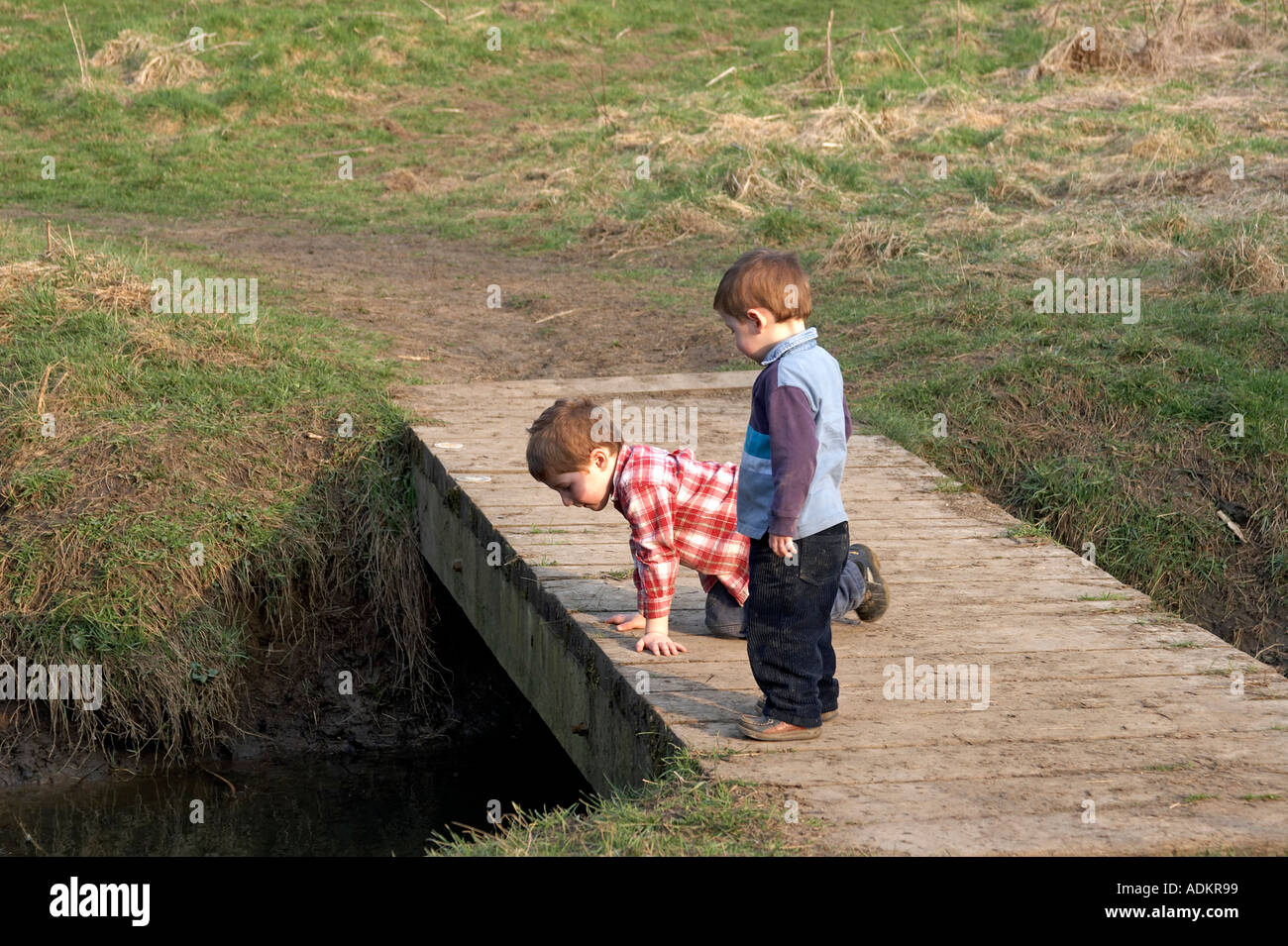 Two young boys children brothers on a bridge over a stream playing poo ...