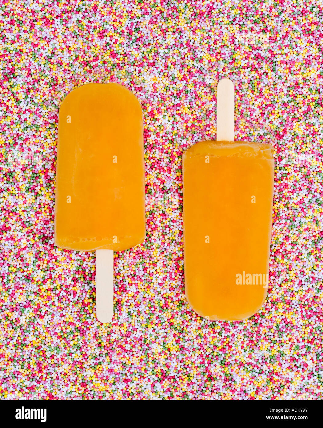 Two orange ice lollies on hundreds and thousands cake sprinkles ...
