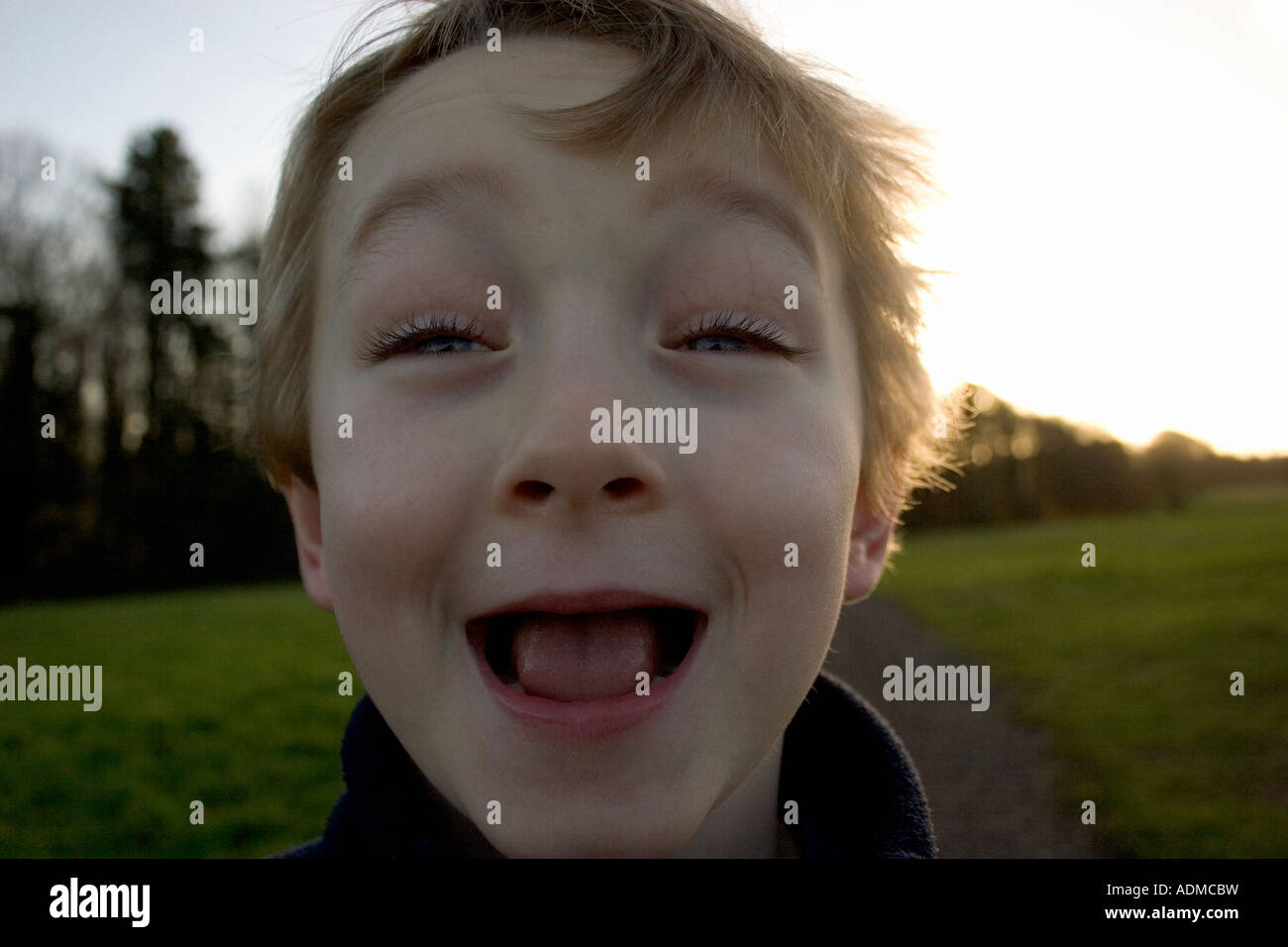 Boy 5-6 years pulling a funny playful face shouting in the park at ...