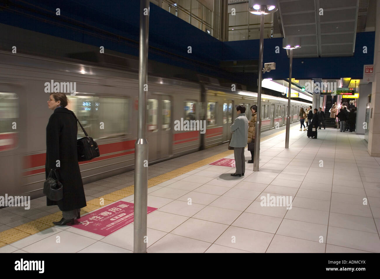 People stand on the platform at a subway station in Yokohama, Japan ...