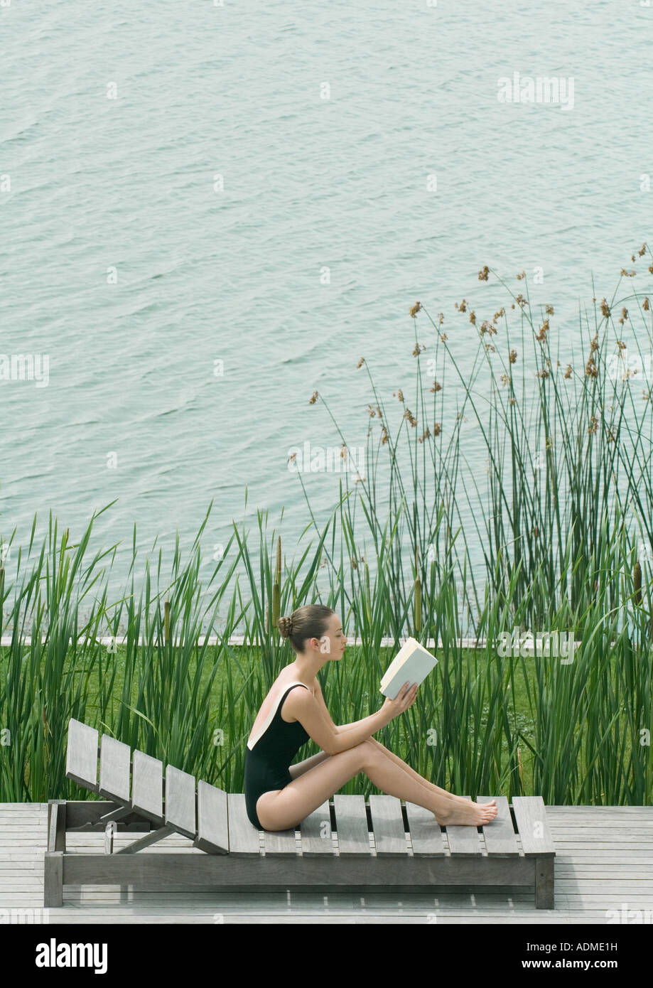 Young woman sitting on lounge chair, reading Stock Photo - Alamy