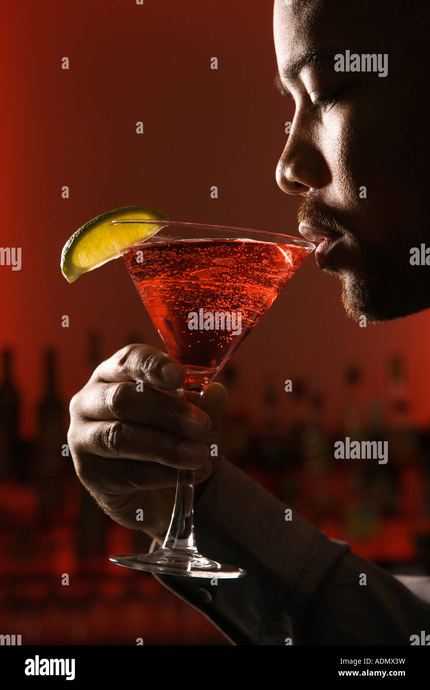 African American man drinking martini in bar against glowing red ...
