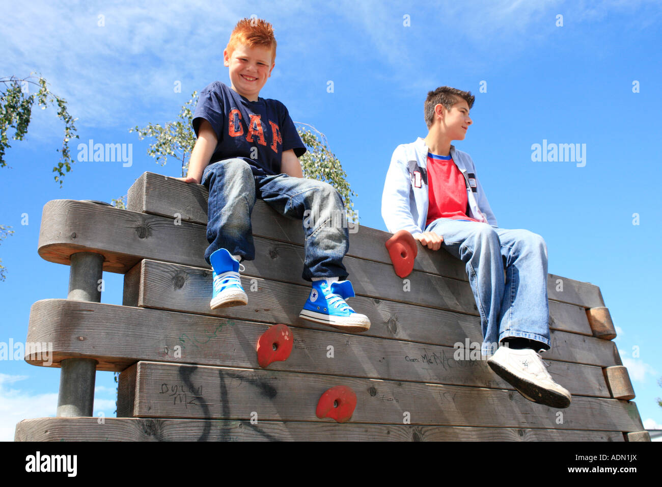 two young boys sitting on a climbing wall at a playground in the suburb ...