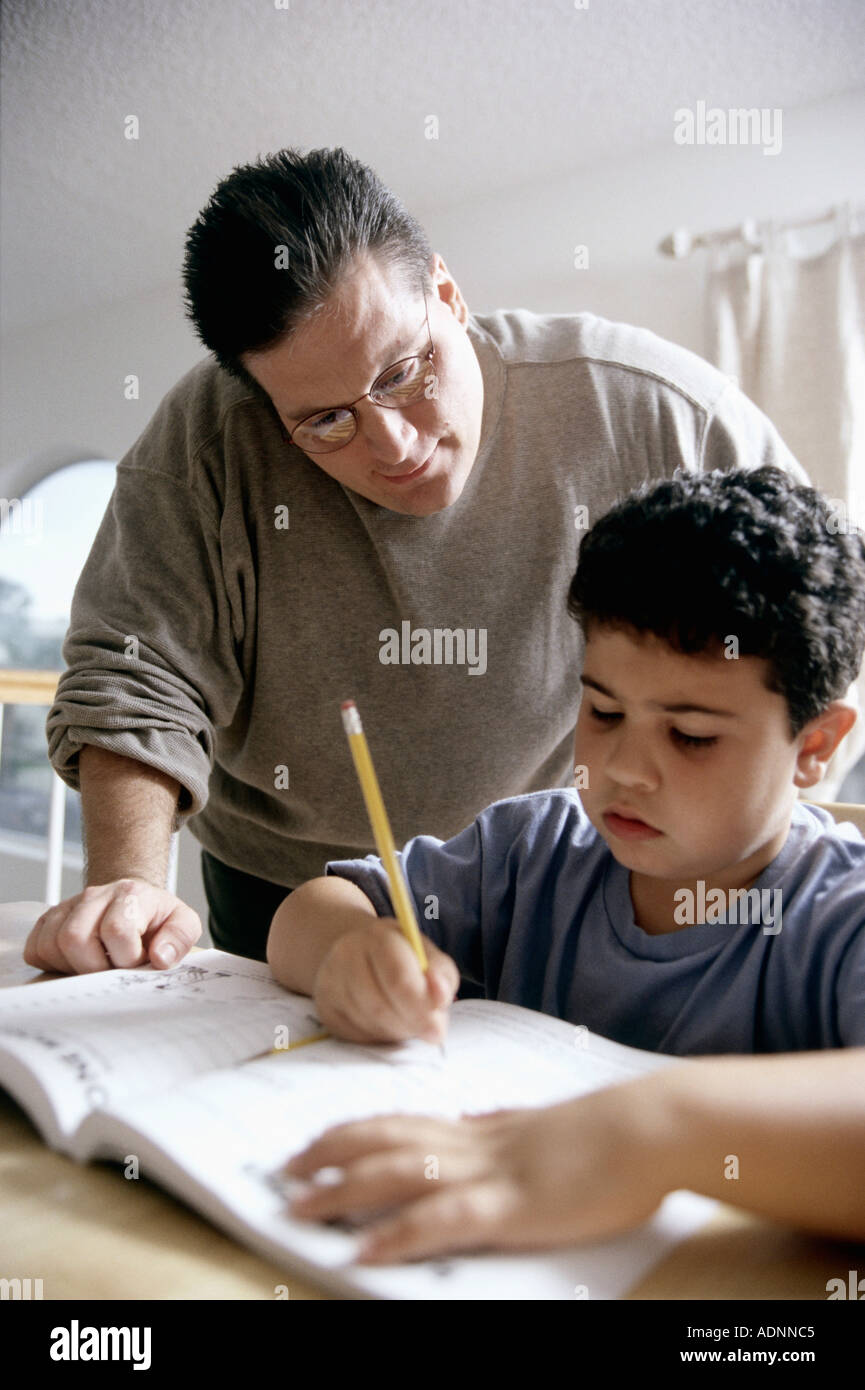 Boy writing in a book with his father standing beside him Stock Photo ...