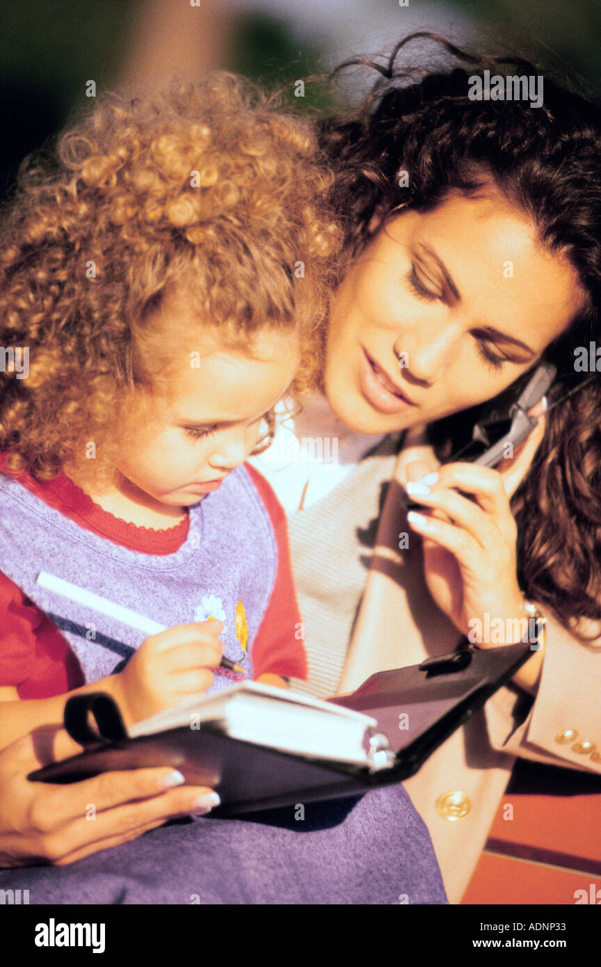 Mother talking on a mobile phone with her daughter standing beside her ...