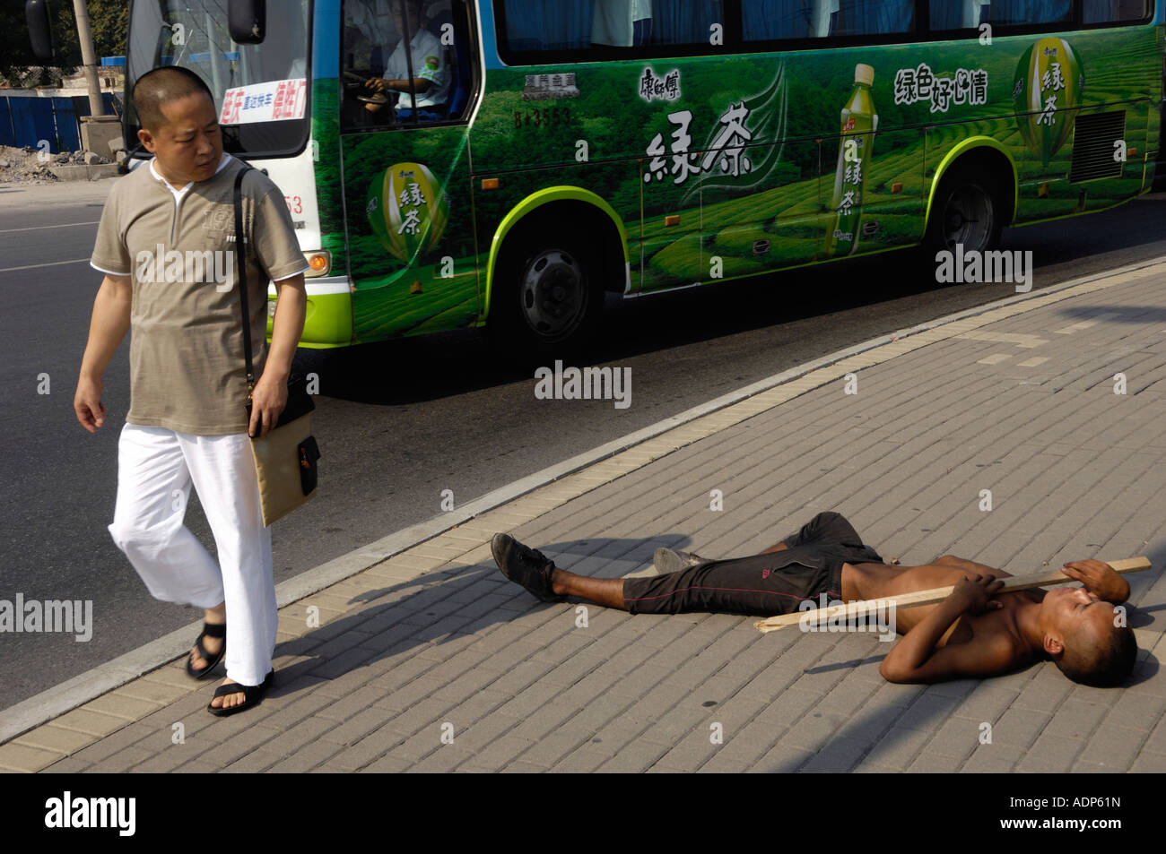A man walks past a young beggar lying on the roadside in Beijing China ...