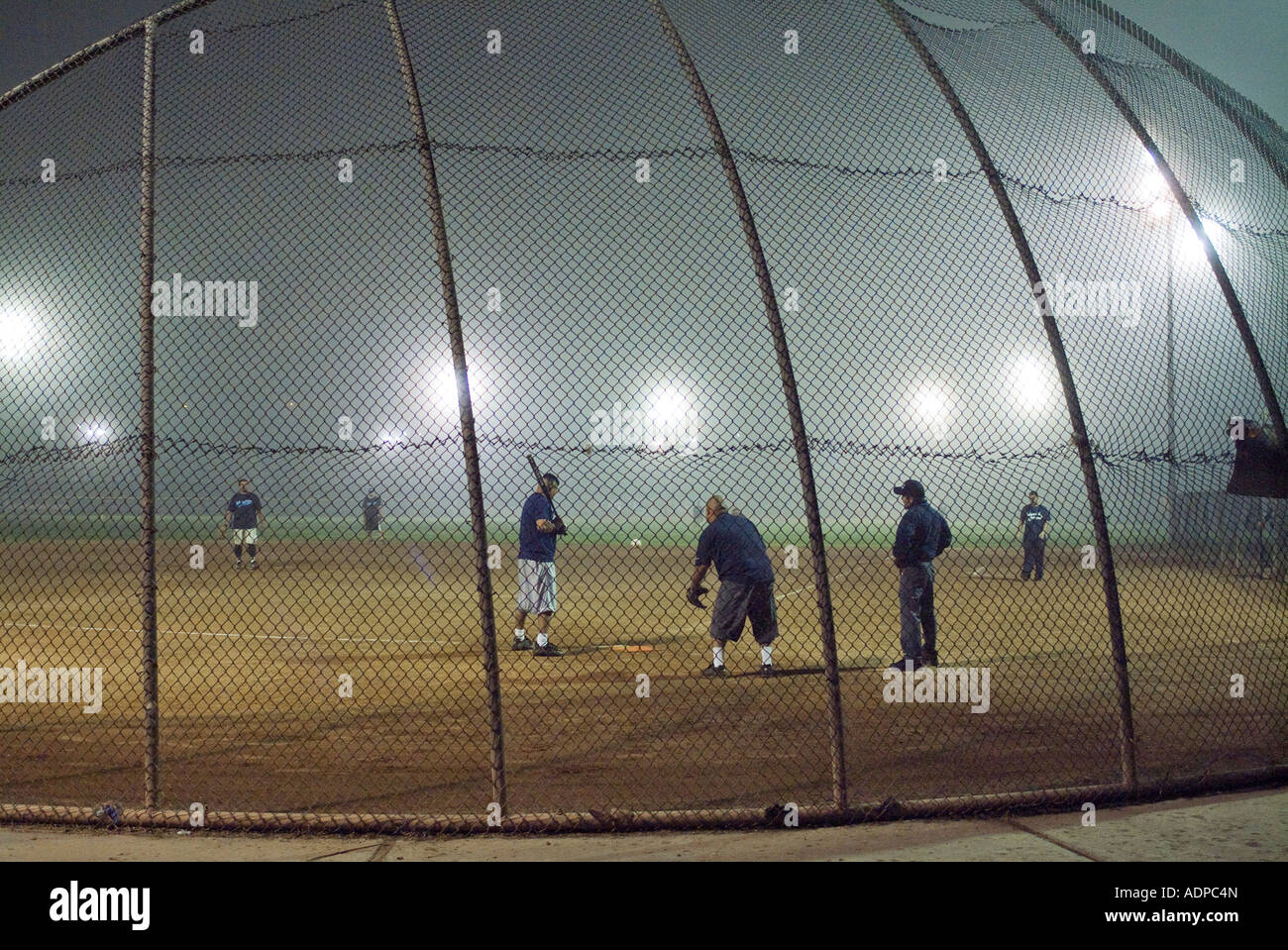 Mens softball team playing at night on a field surrounded by an eerie ...