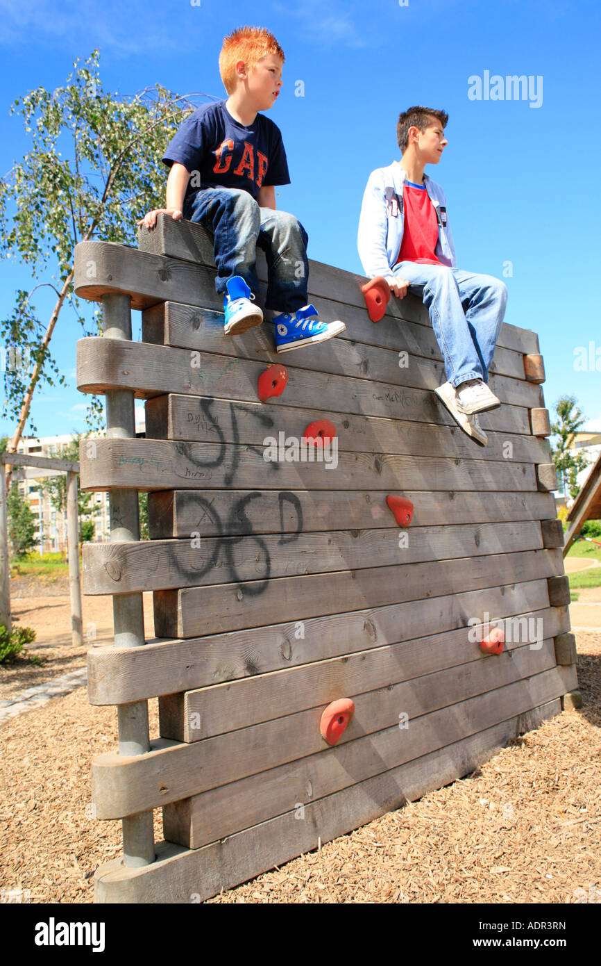 two young boys sitting on a climbing wall at a playground in the suburb ...