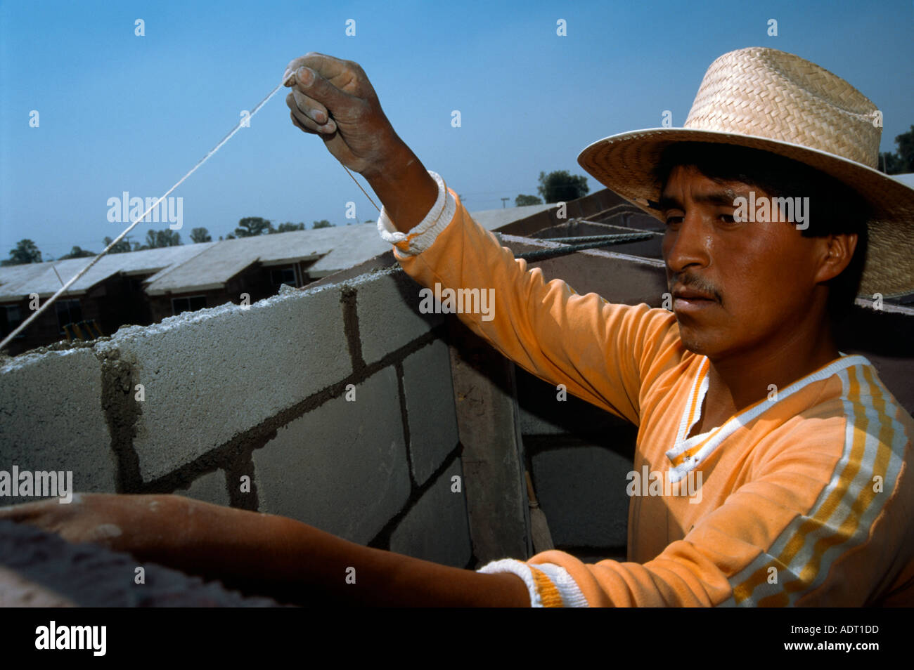 A construction worker levels a row of cement blocks with a string for a ...