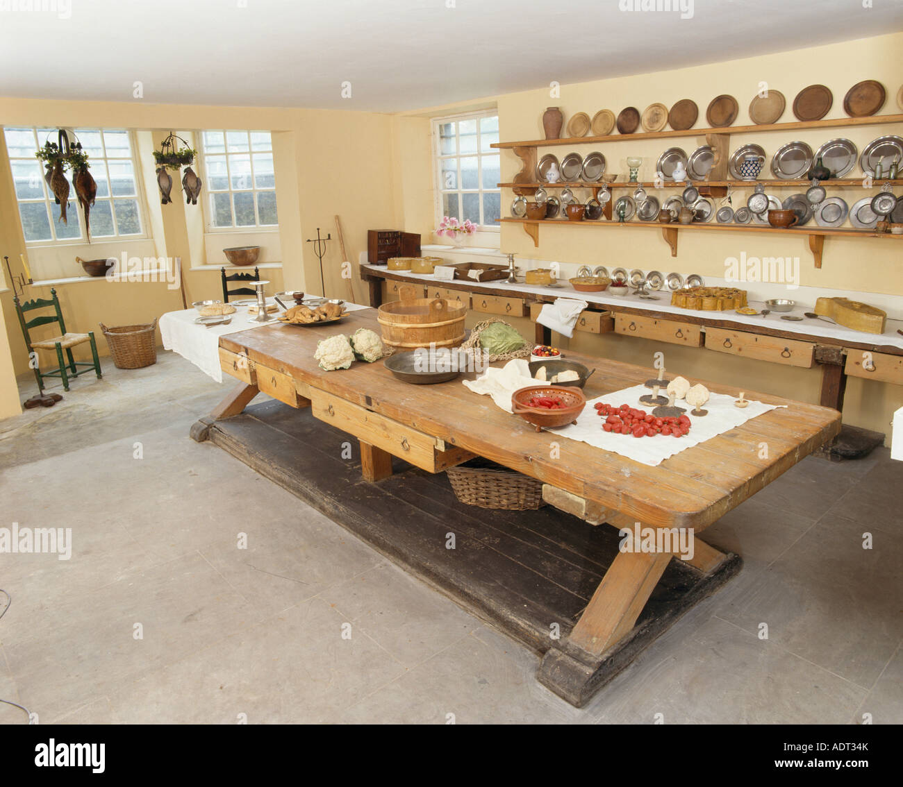 Large Edwardian kitchen with cookery preparation on long wooden table ...