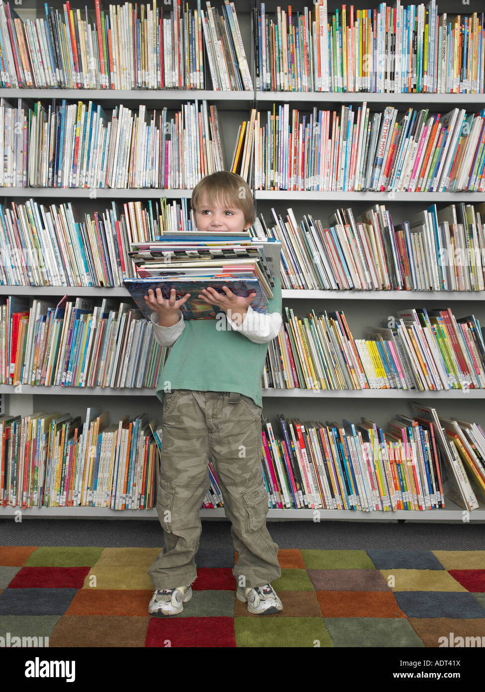 Boy holding stack of books in front of library bookshelf Stock Photo ...