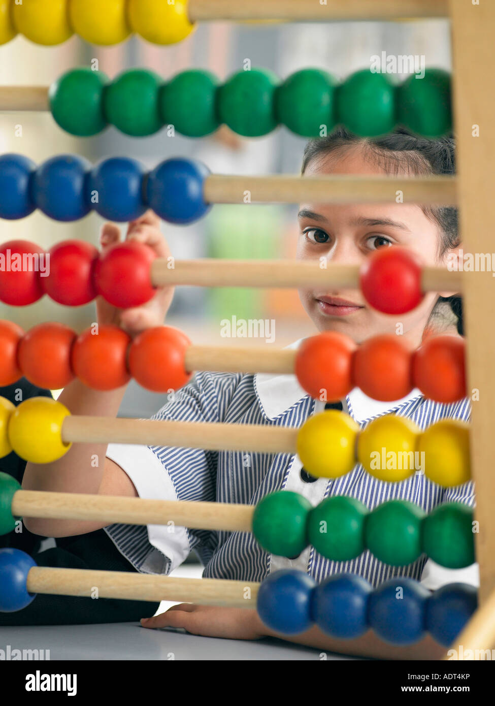 Elementary schoolgirl looking through abacus, sitting in classroom ...