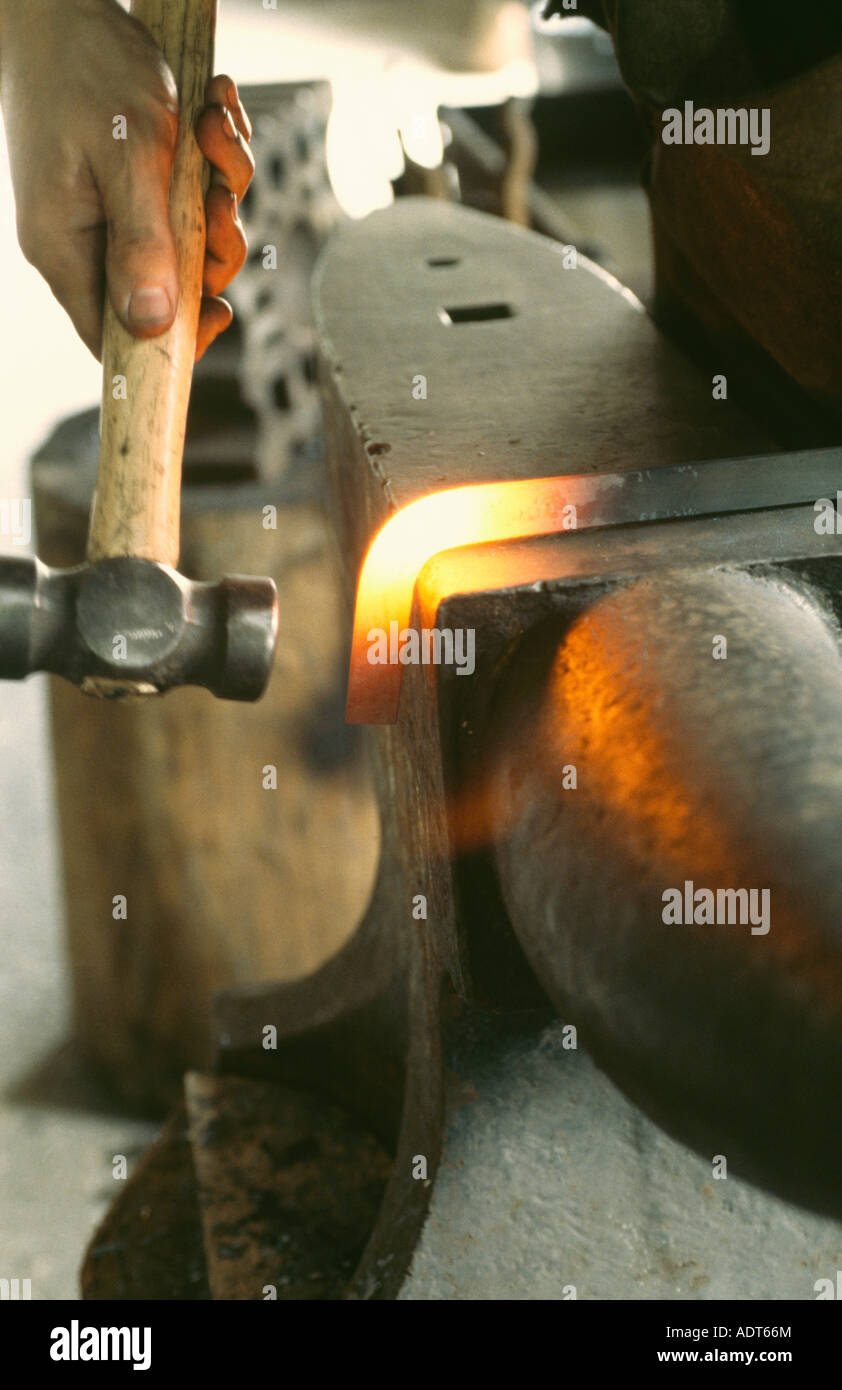 Close-up of hand using hammer to forge red hot steel on the anvil in a ...