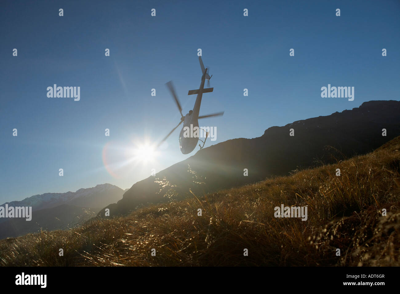 Helicopter flying over hills in front of the sun Stock Photo - Alamy