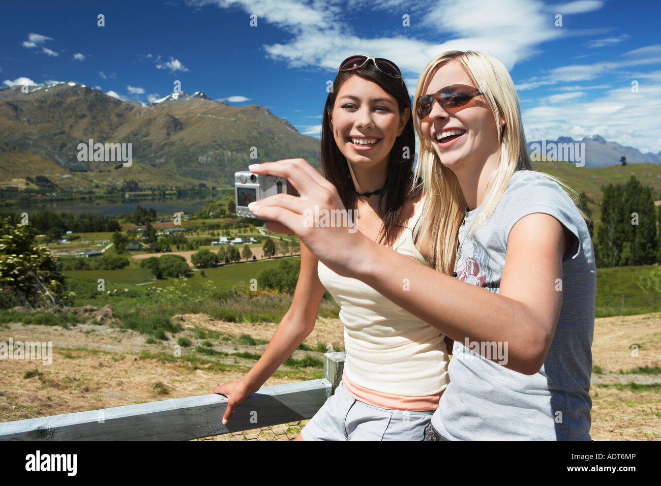Two women taking picture against fence with mountains behind Stock ...