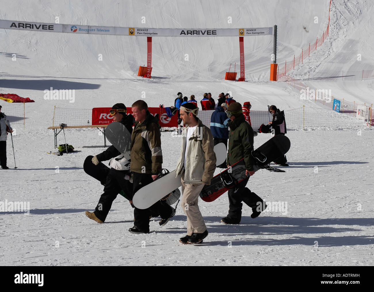 Four young male snowboarders walk across the snow at the bottom of the ...