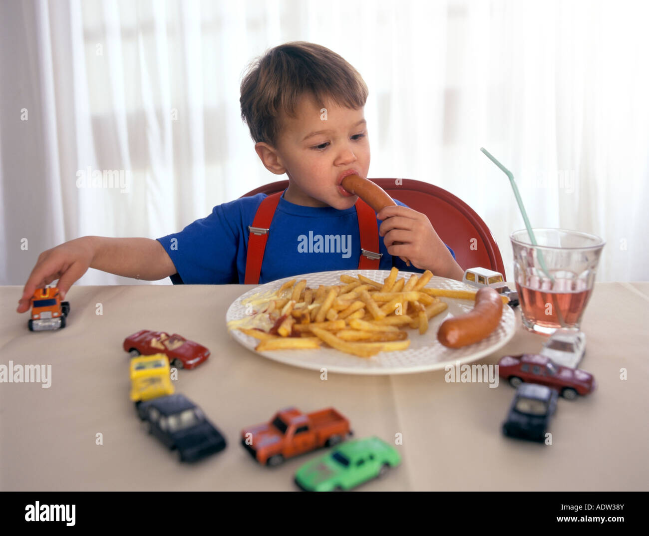 Little boy is eating french fries and sausages and playing with toy ...