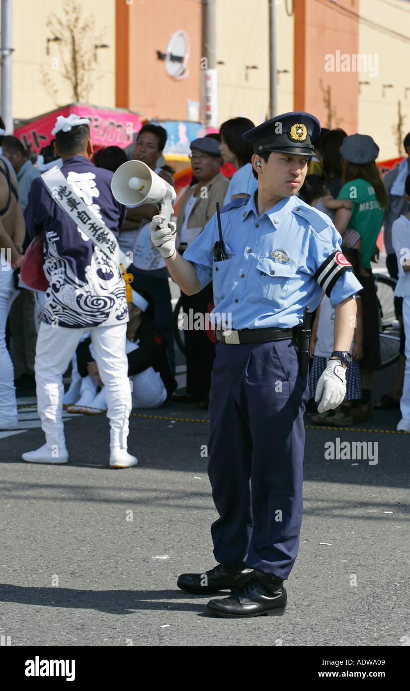 A Japanese policeman in summer uniform patrols a festival in Osaka ...