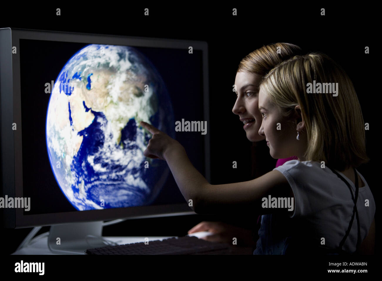 Two girls looking at earth on computer monitor Stock Photo - Alamy