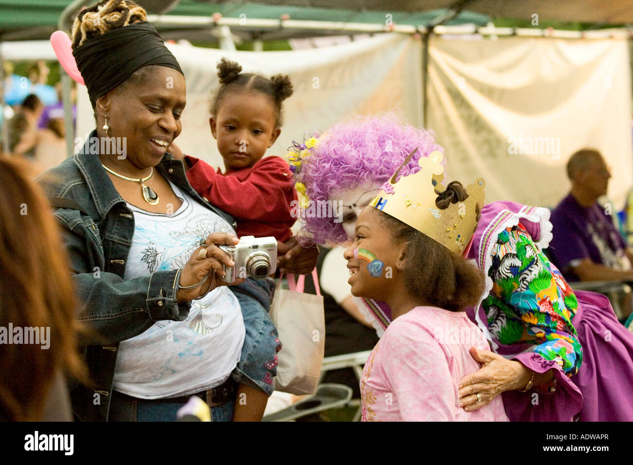 Woman looks at camera image as daughter has face painted by clowns at ...