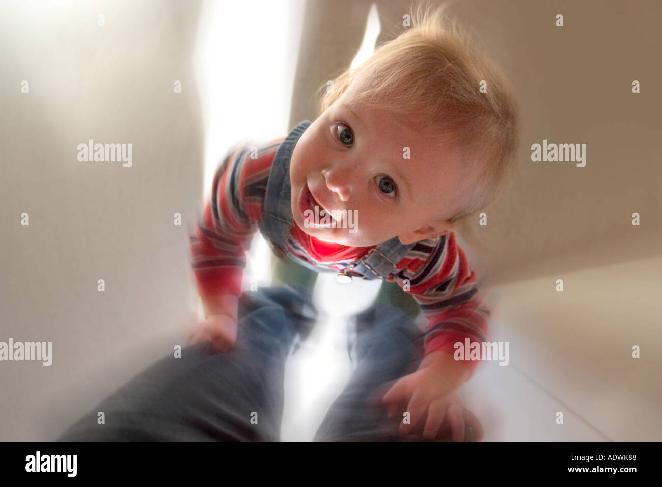 A smiling one year old learns to stand by holding on to mother's legs ...