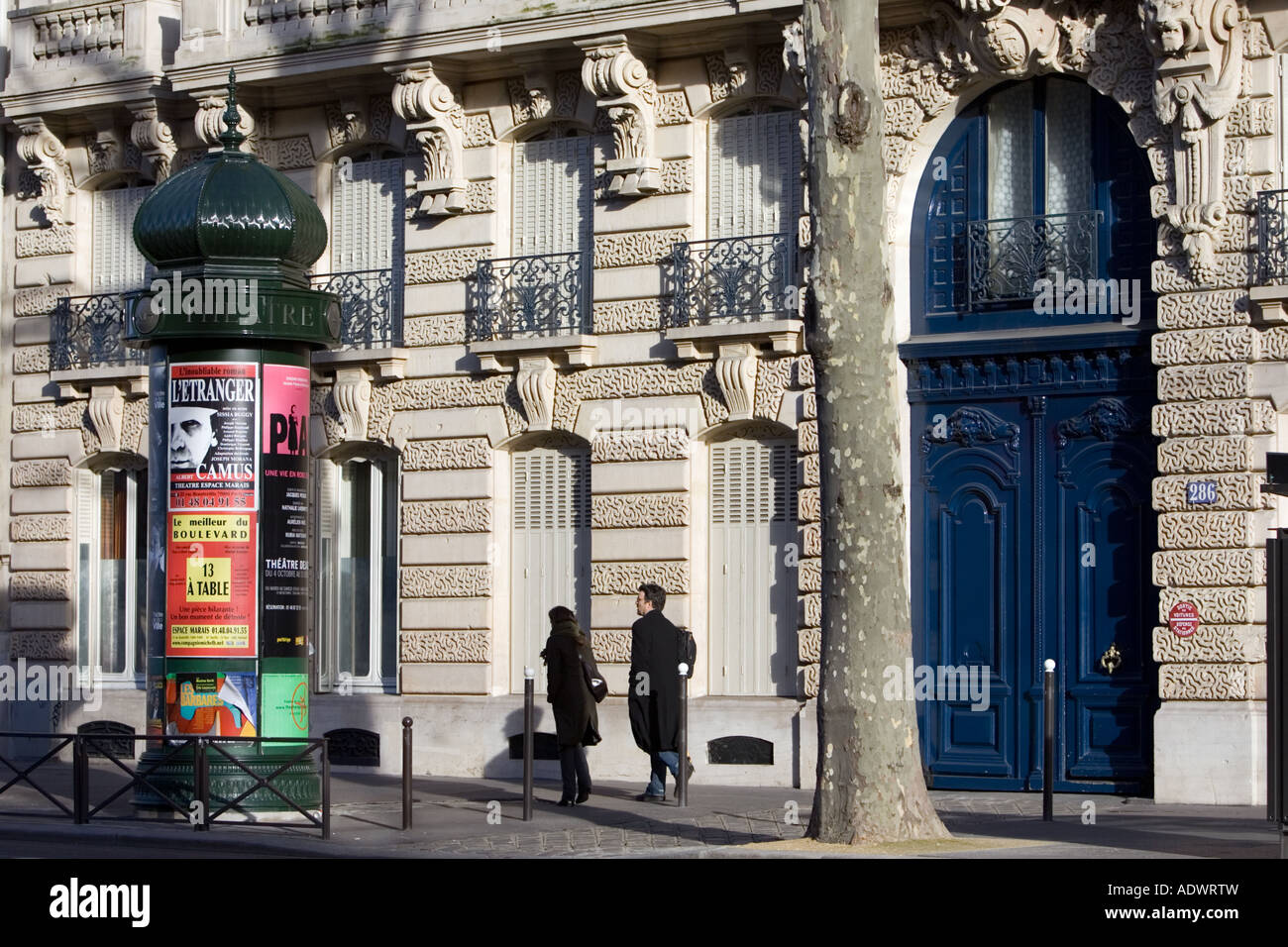 Couple walk past obelisk advertising theatre productions in Parisian ...