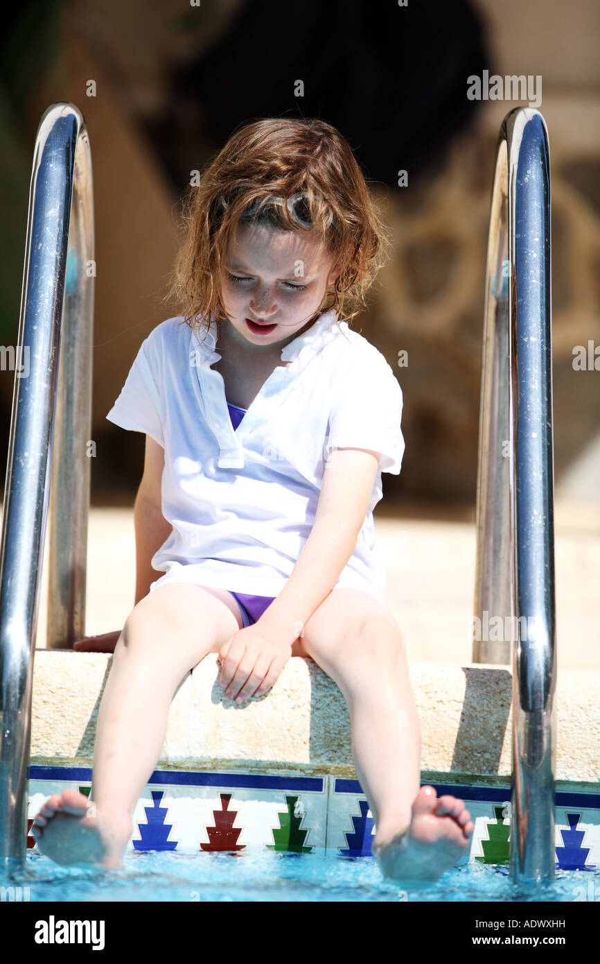 Young girl sitting on the edge of a swimming pool splashing water with ...