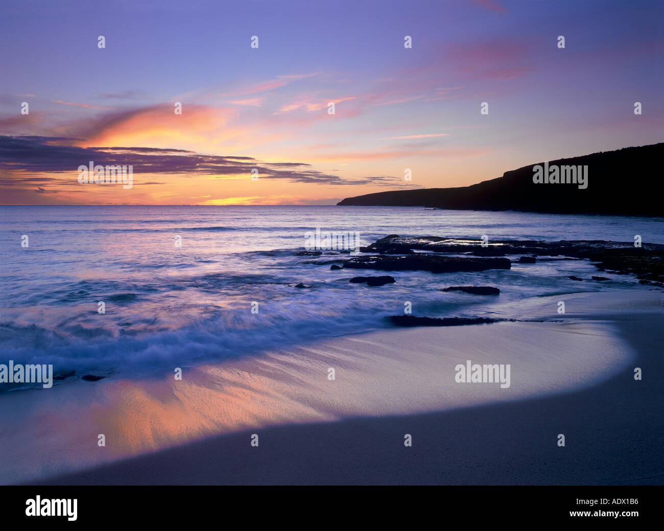 Beach with rocks and glowing sky reflecting on water Stock Photo - Alamy