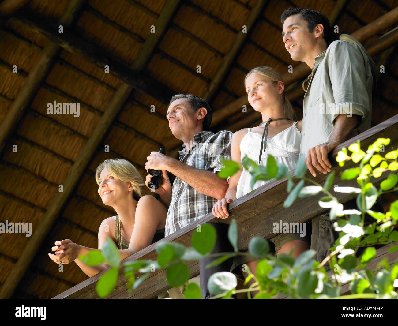 Four people looking at view from terrace, man holding binoculars, low ...